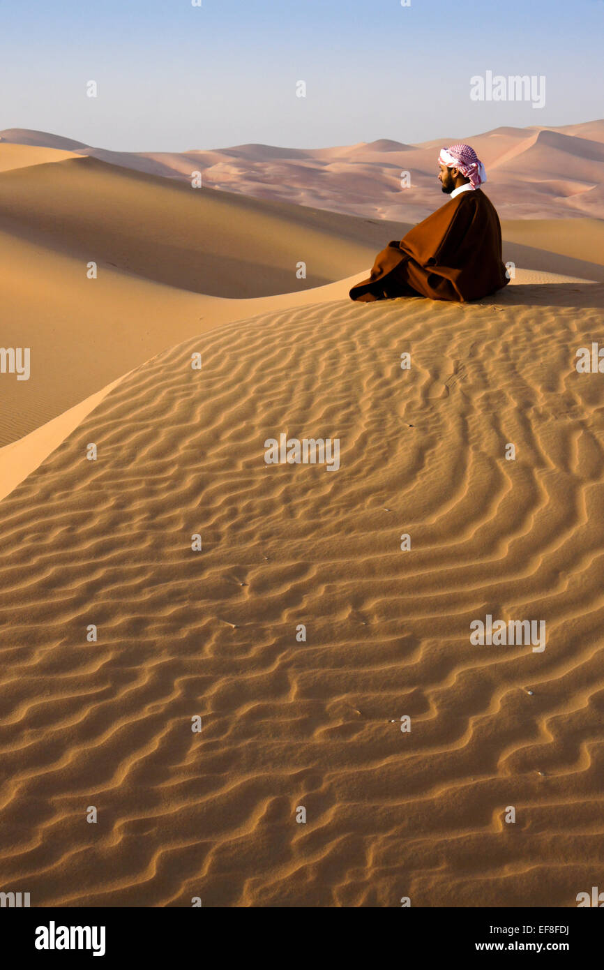 Man in traditional dress sitting in sand dunes of Liwa, Abu Dhabi, UAE ...