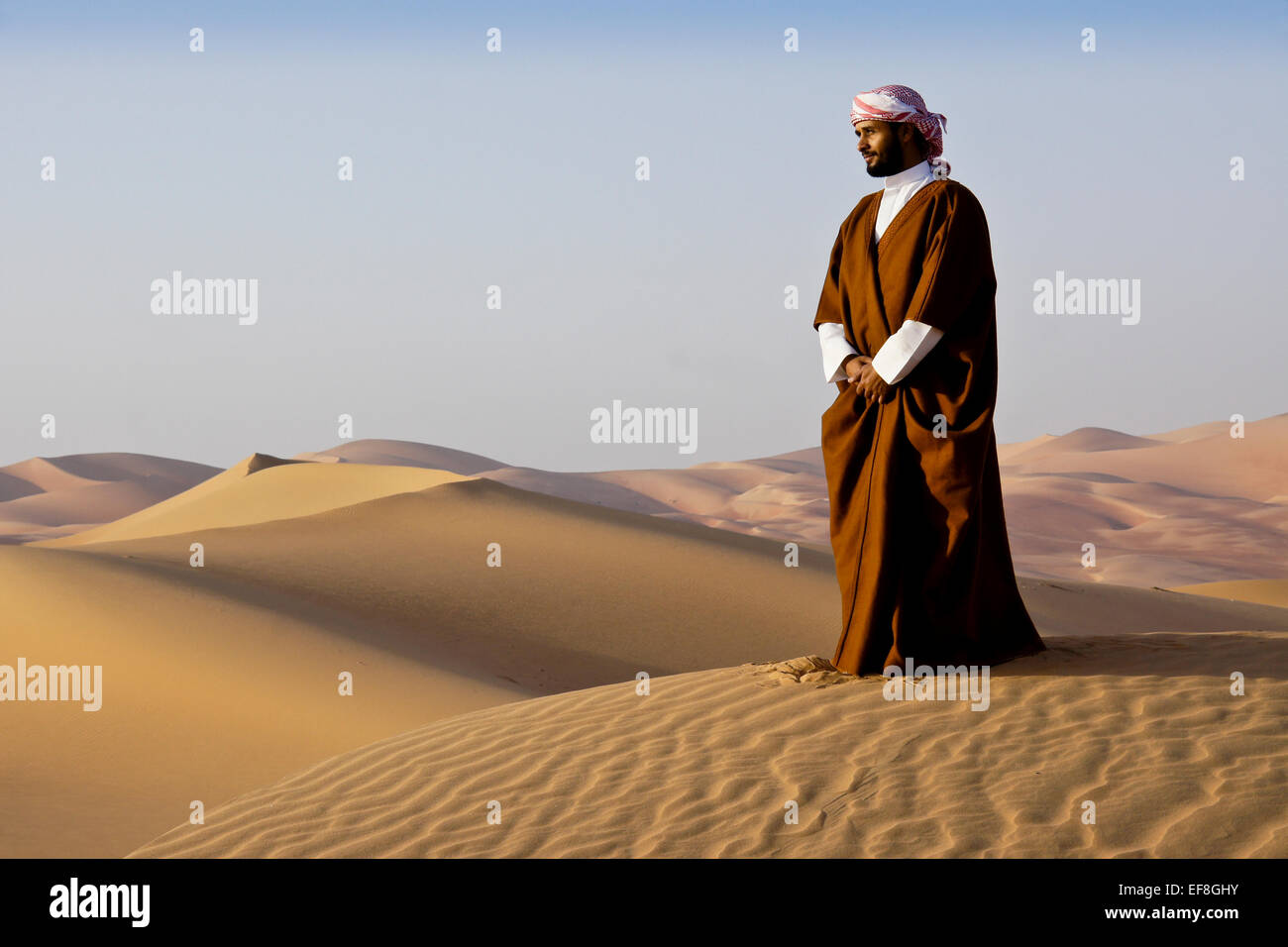 Man in traditional dress standing in sand dunes of Liwa, Abu Dhabi, UAE ...