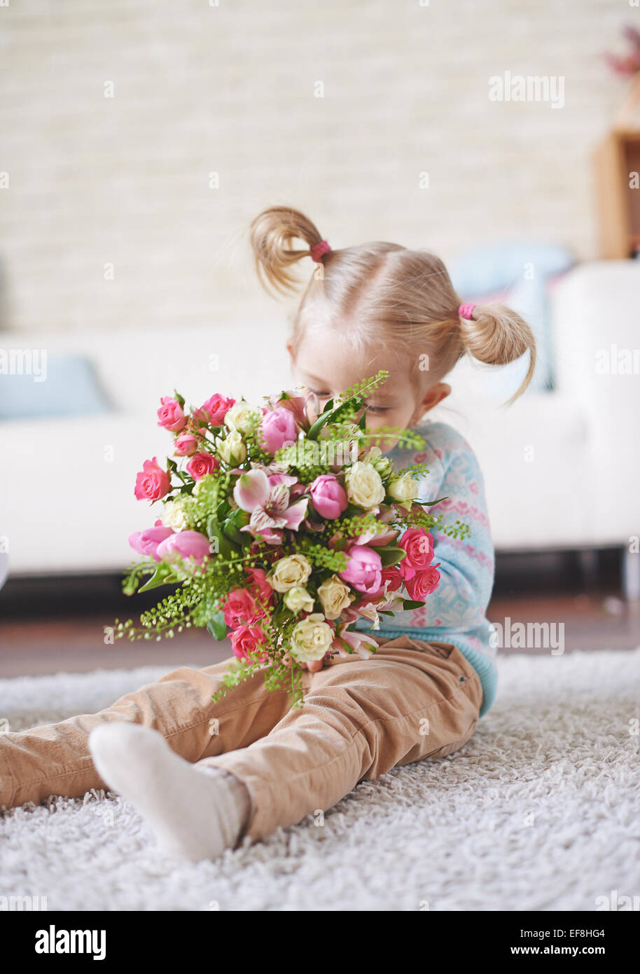 Adorable child smelling fresh flowers while sitting on the floor Stock ...