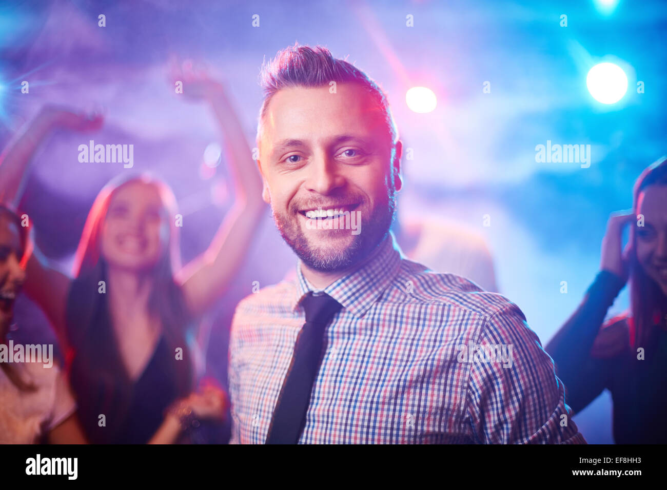 Handsome guy looking at camera at disco while his friends dancing on background Stock Photo - Alamy