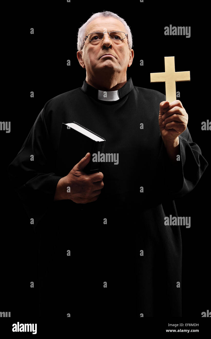 Vertical shot of a mature priest holding a cross and looking up on ...