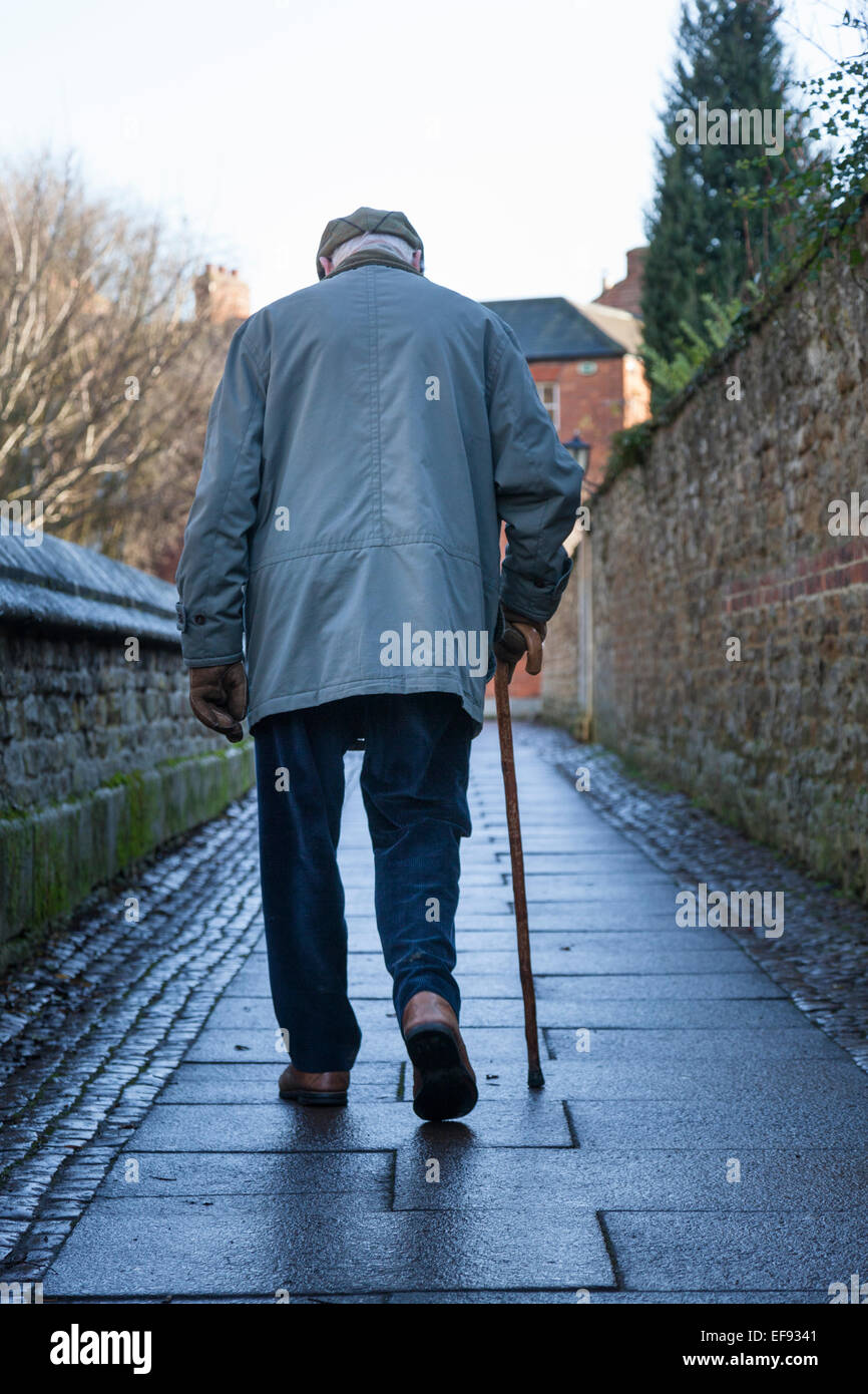 An elderly man with a walking stick walks along a damp path of paving ...