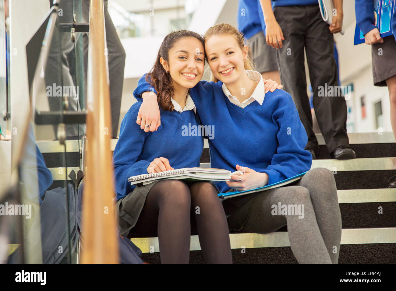 Portrait of two cheerful female students sitting on steps with arms ...