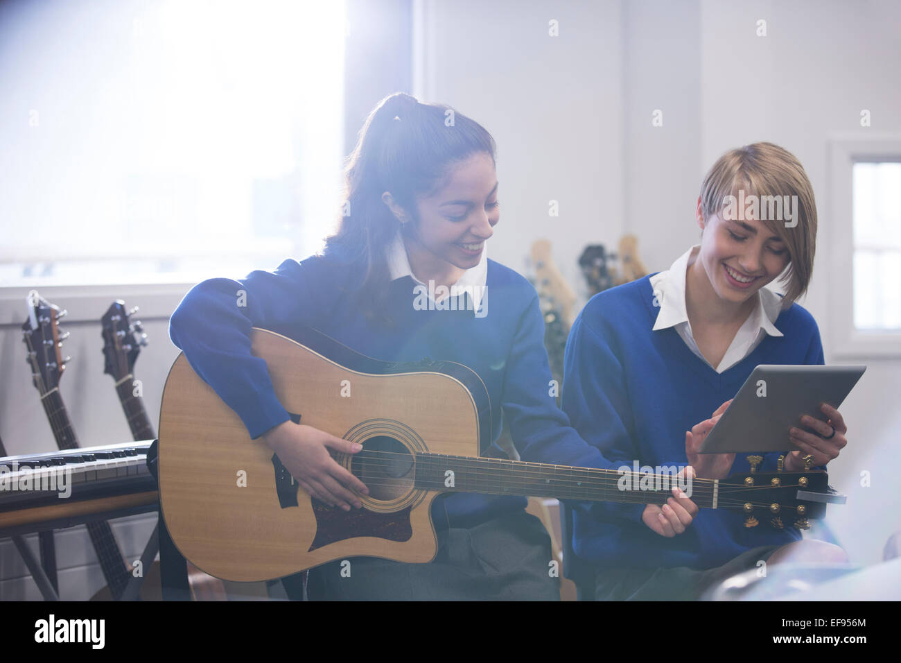 Female students playing acoustic guitar in classroom and using tablet ...