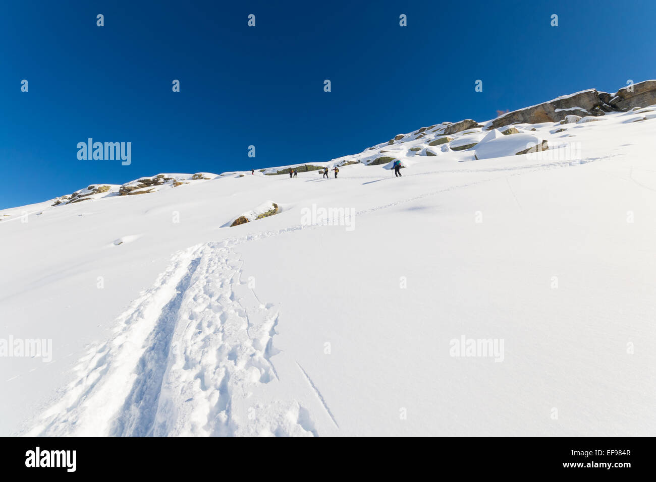 Group of tour skier hiking uphill on a steep snowy slope. Ski tracks in ...