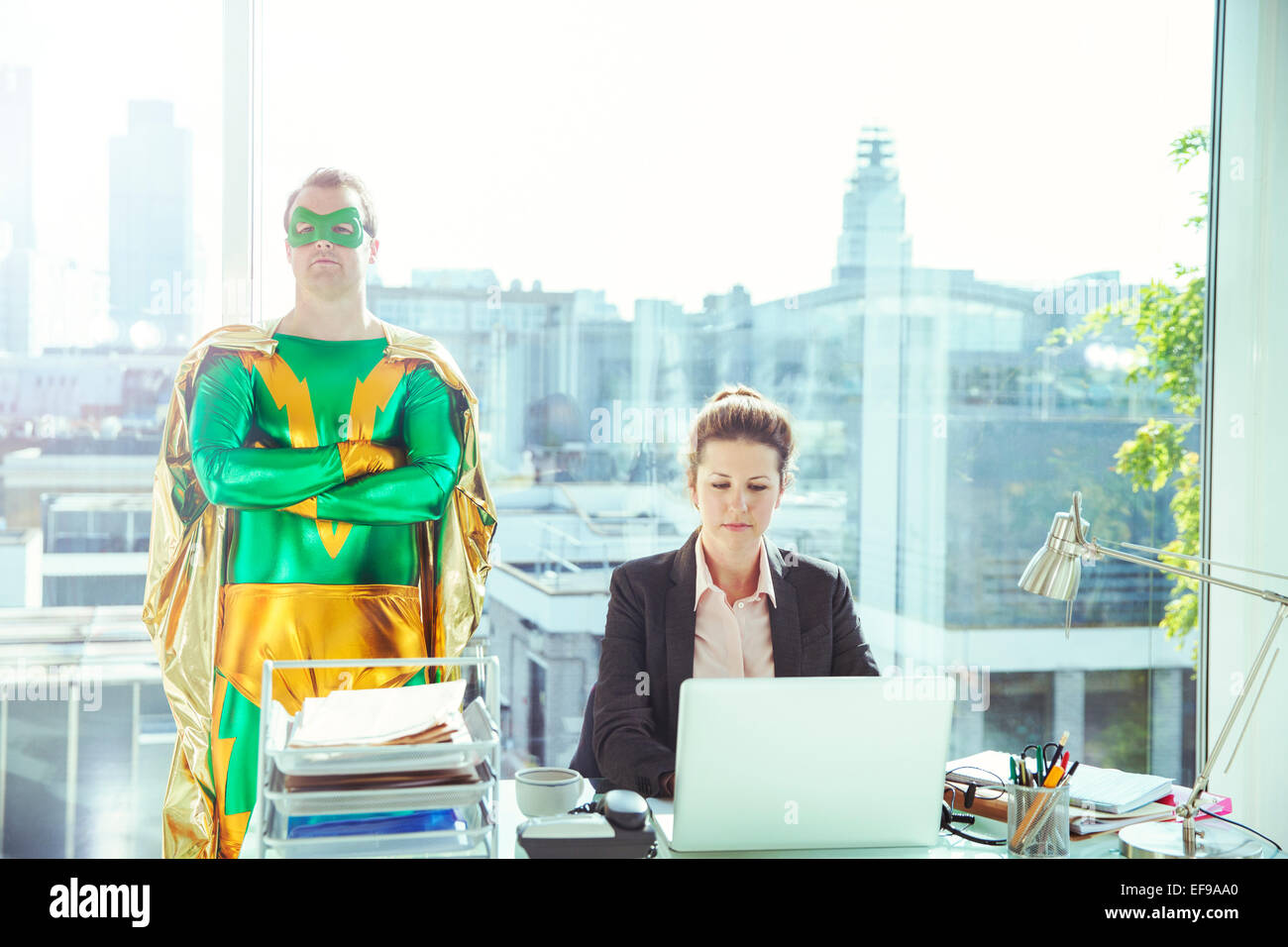 Superhero standing near businesswoman working in office Stock Photo - Alamy