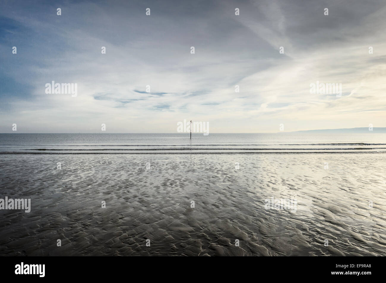 A wide angle seascape beach with a tide marker visible centrally. The ...