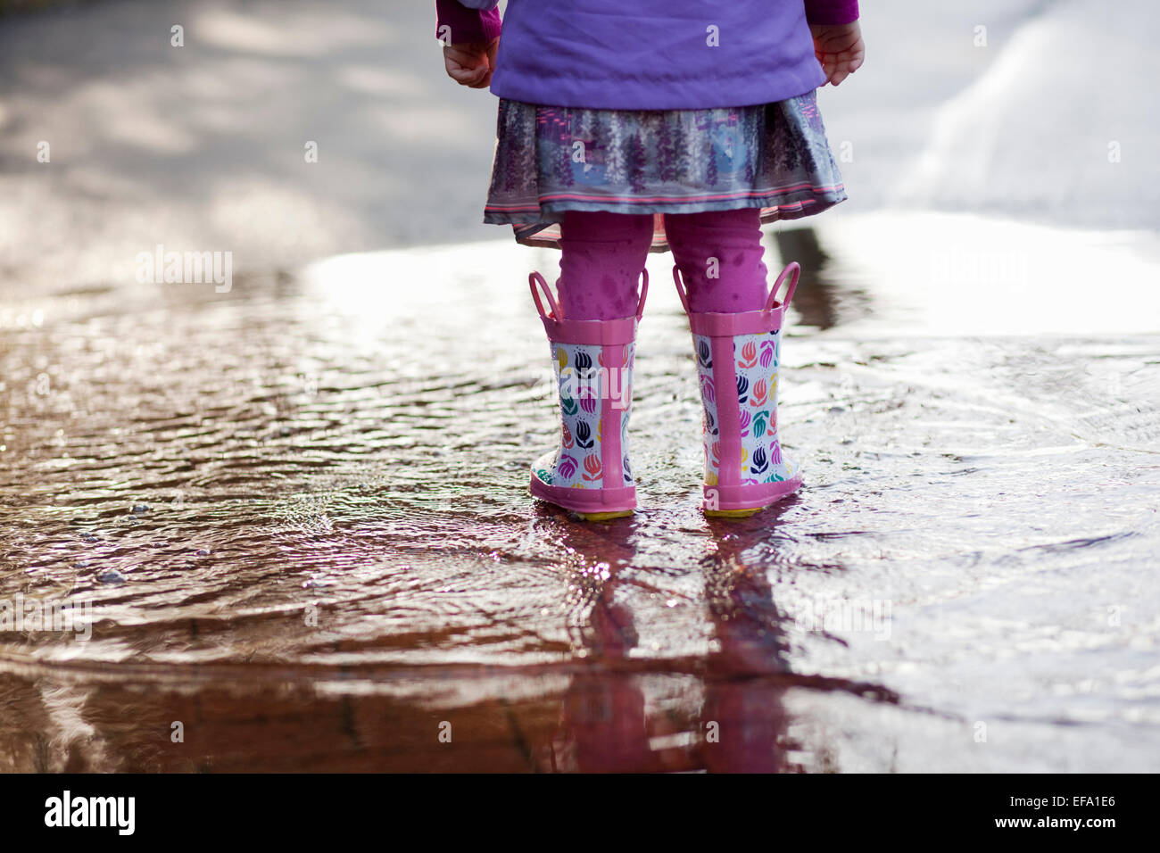 A little girl wearing rain boots stands in a puddle on the street Stock ...