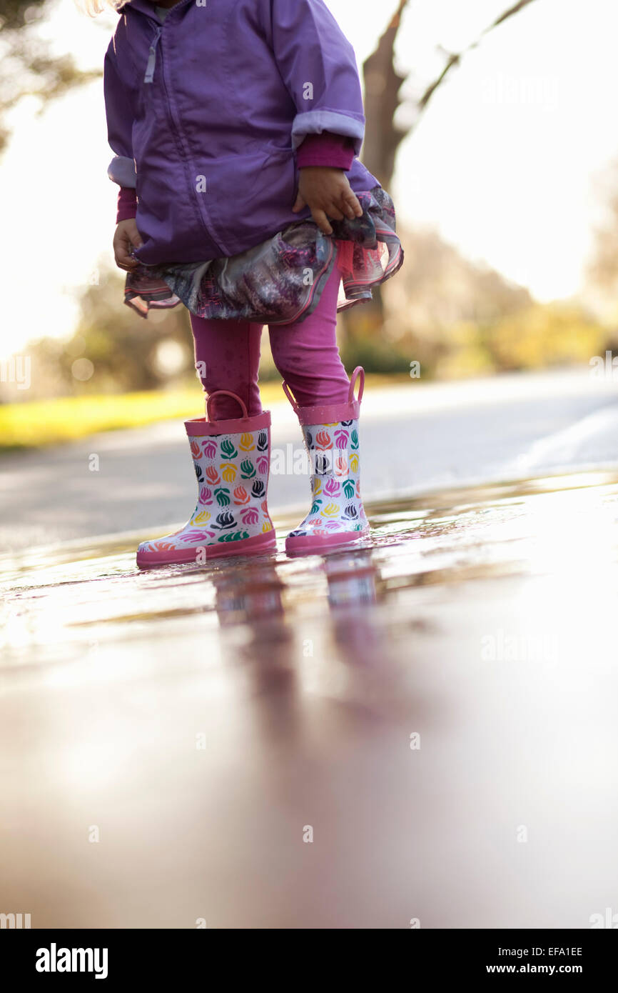 A little girl wearing rain boots stands in a puddle in the street Stock Photo - Alamy