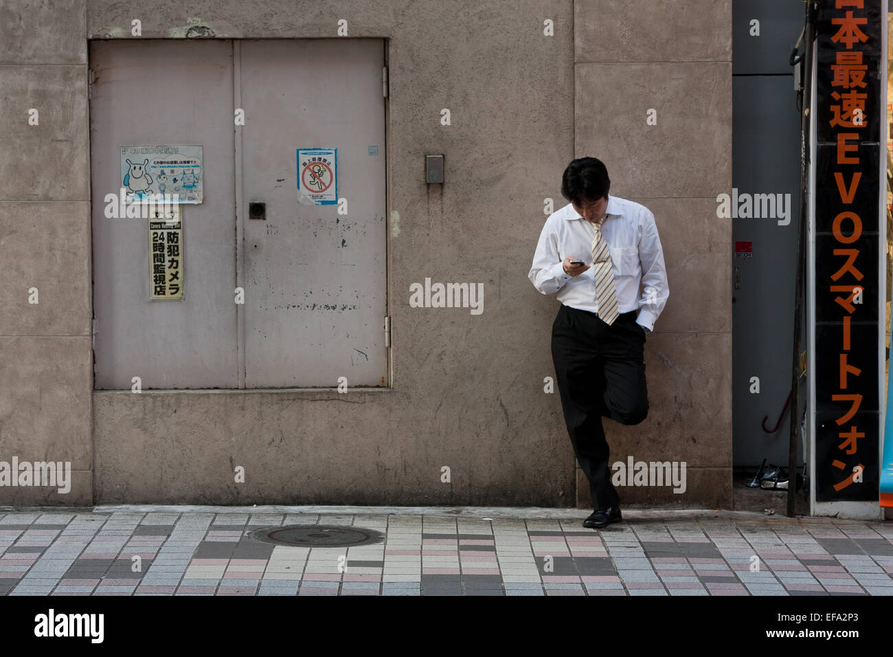 A Japanese salaryman or male office worker leans against a wall as he ...