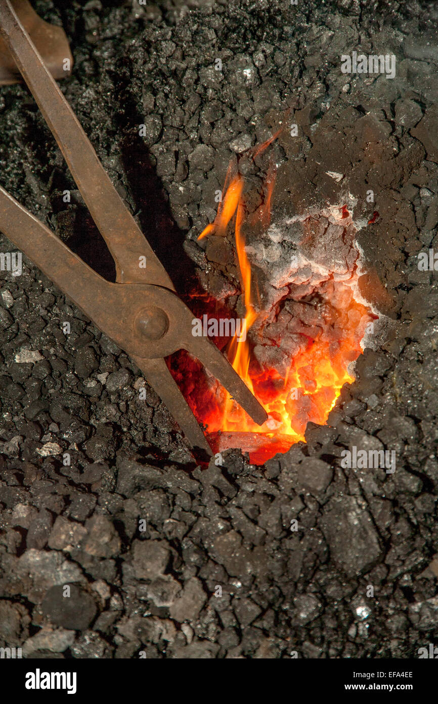 Pincers hold iron being heated red-hot in the coal-fired forge of a ...