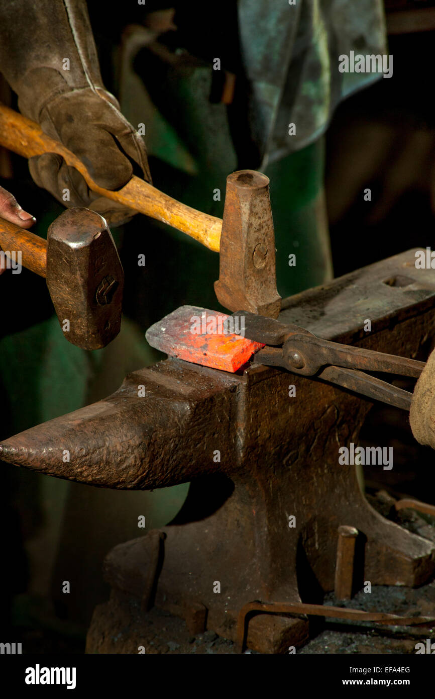 A blacksmith's hammers shape red-hot iron being held with pincers on ...