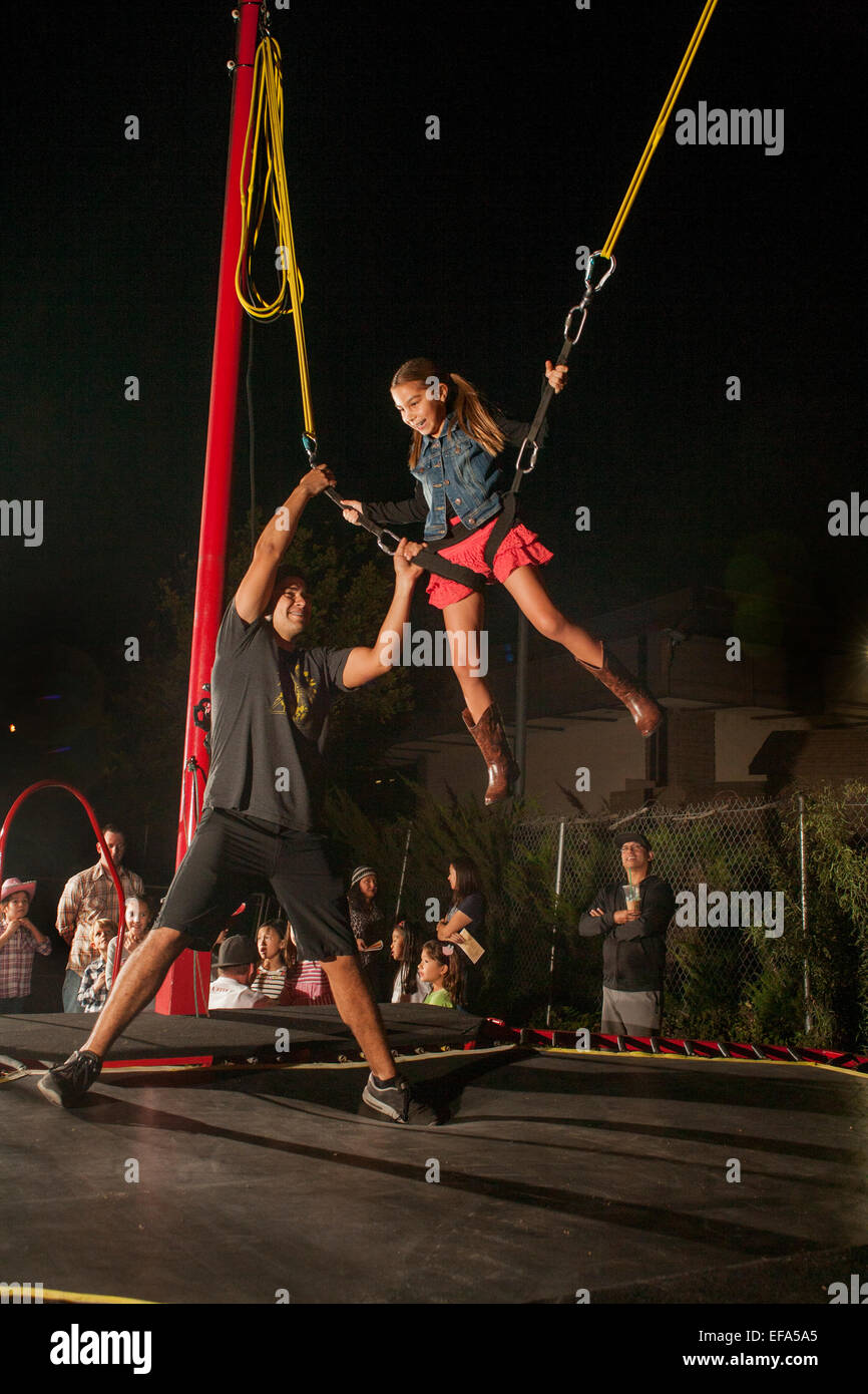 A girl does tethered bungee jumping over a trampoline during an evening ...