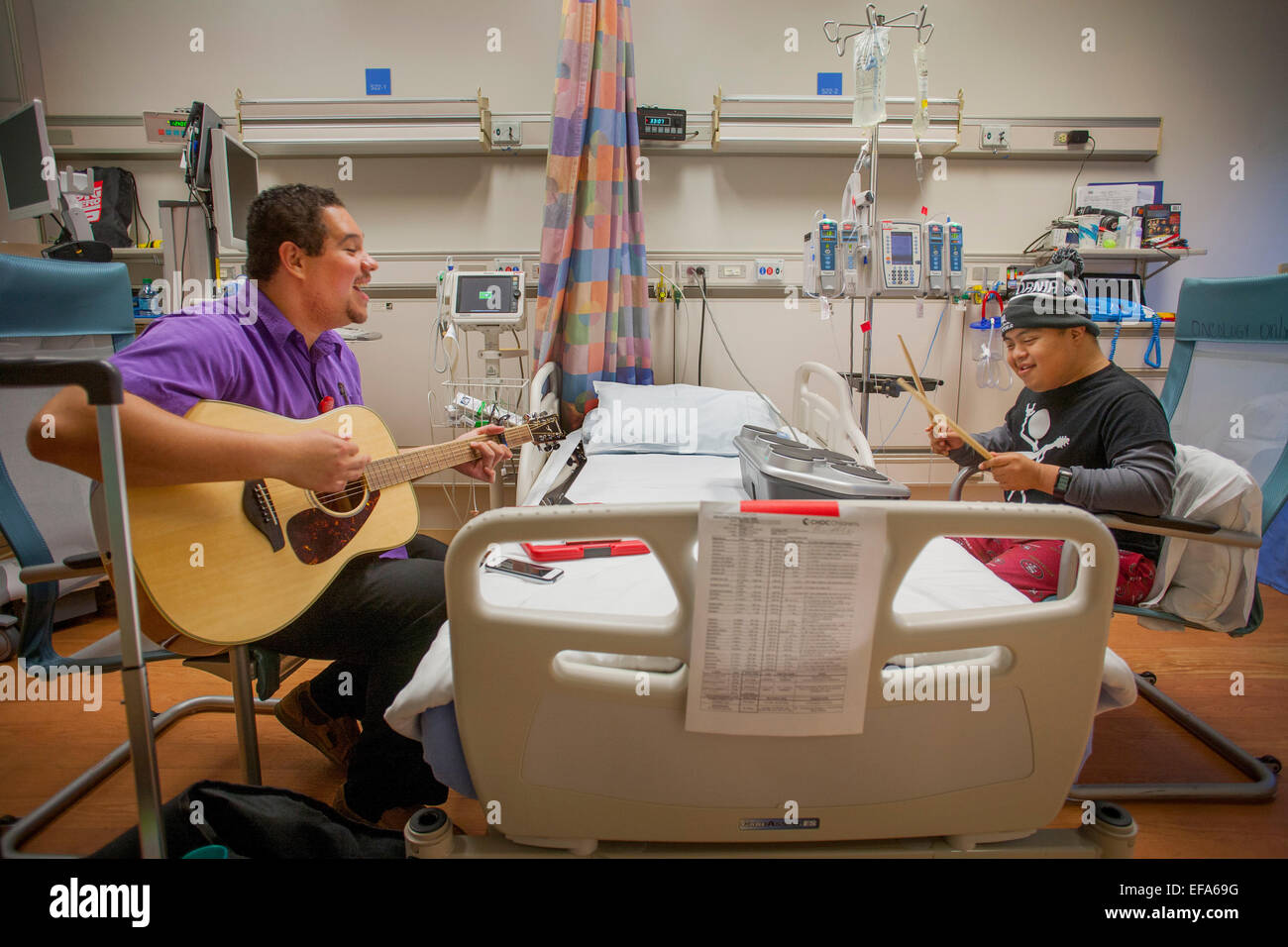 A music therapist playing a guitar entertains a young boy patient at ...