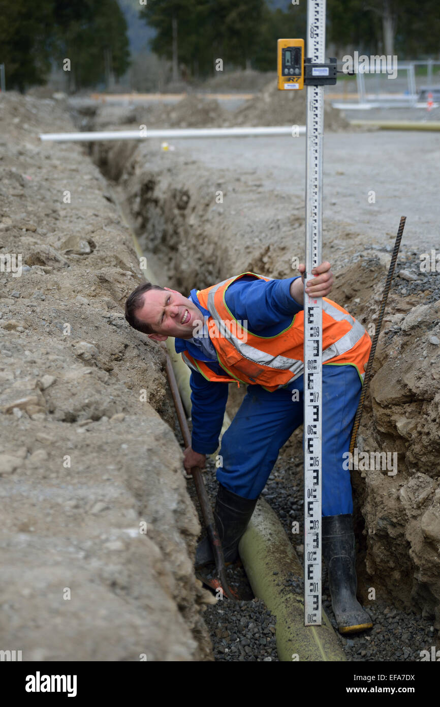 A tradesman uses a laser surveying tool to adjust the depth of his pipe ...