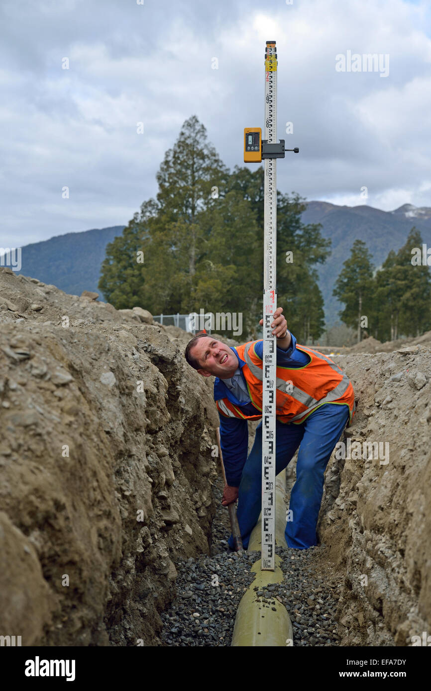 A tradesman uses a laser surveying tool to adjust the depth of his pipe ...
