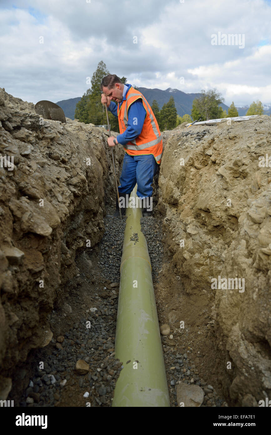 A tradesman packs gravel under a pipe in a new stormwater drain Stock ...