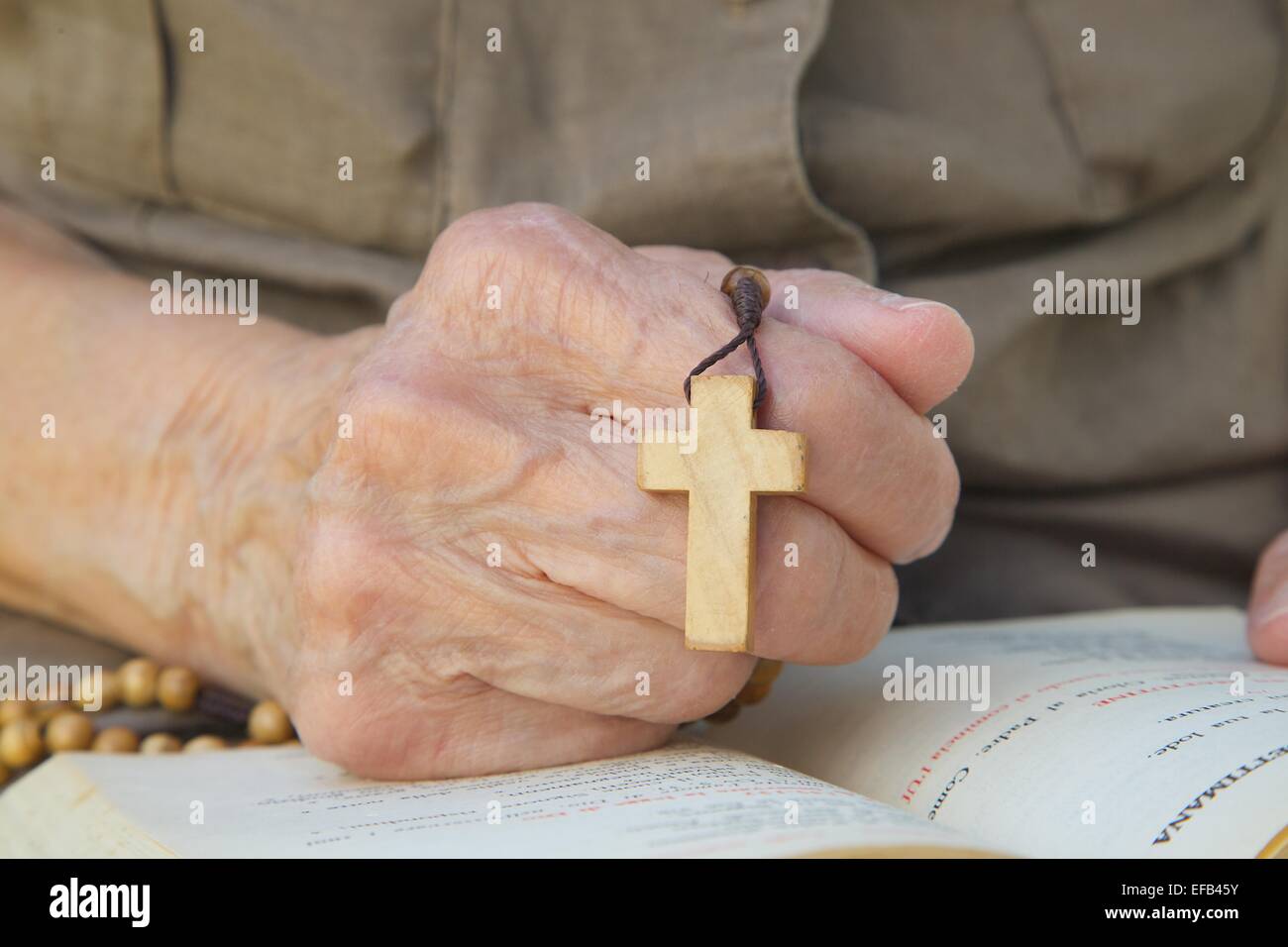 A hand of senior woman with wooden cross on a Franciscan prayer book ...