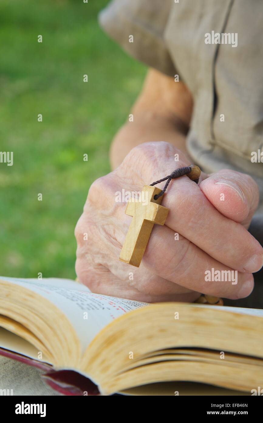 A hand of senior woman with wooden cross on a Franciscan prayer book ...