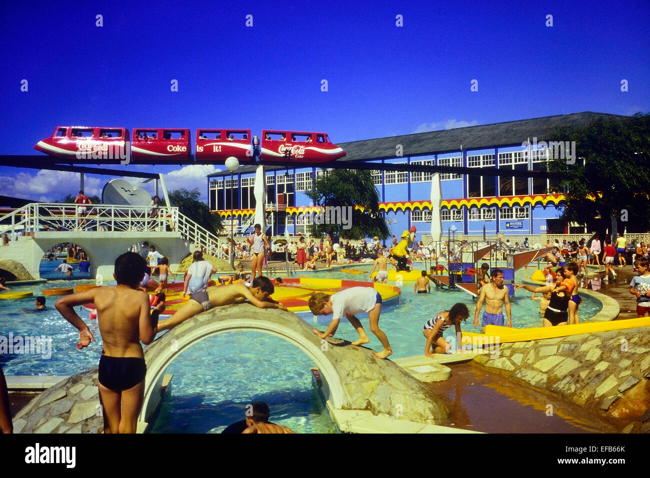 A monorail passes over the sun splash outdoor swimming pool at Butlins ...