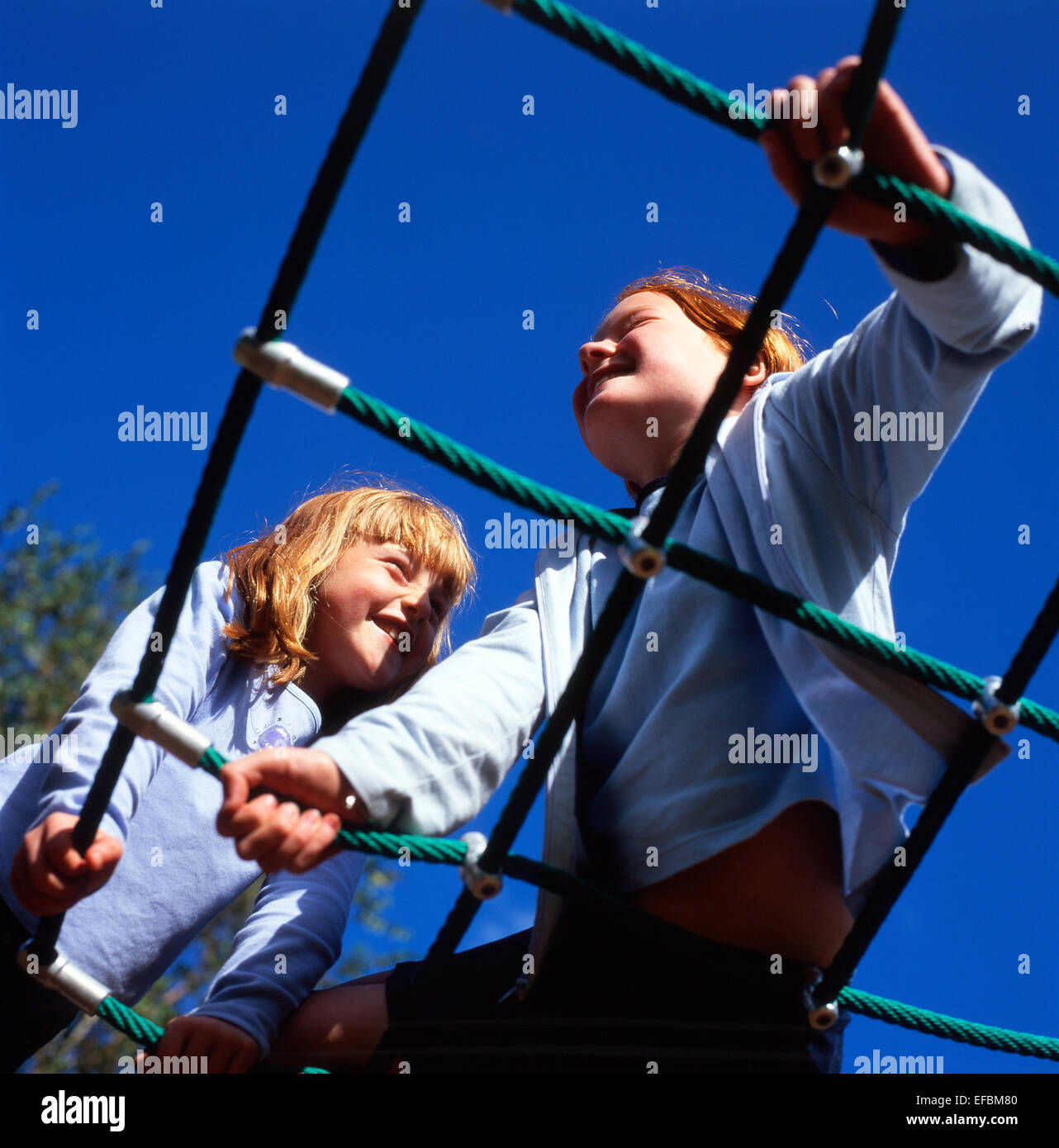 Two girls having fun playing on rope climbing frame in park at Gelli ...