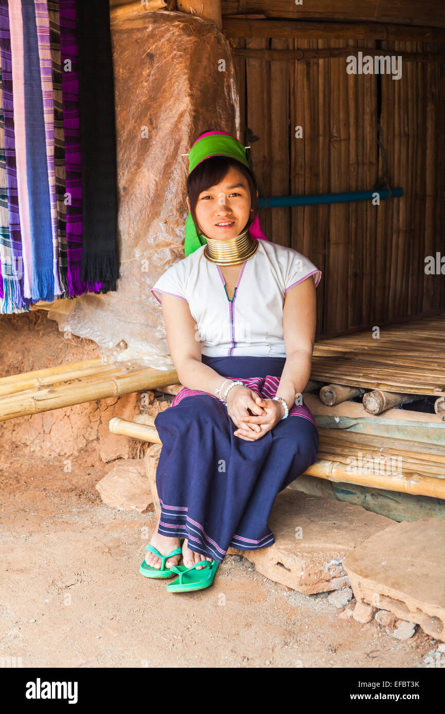 Young Burmese long neck woman with a green headdress sitting in a hut ...