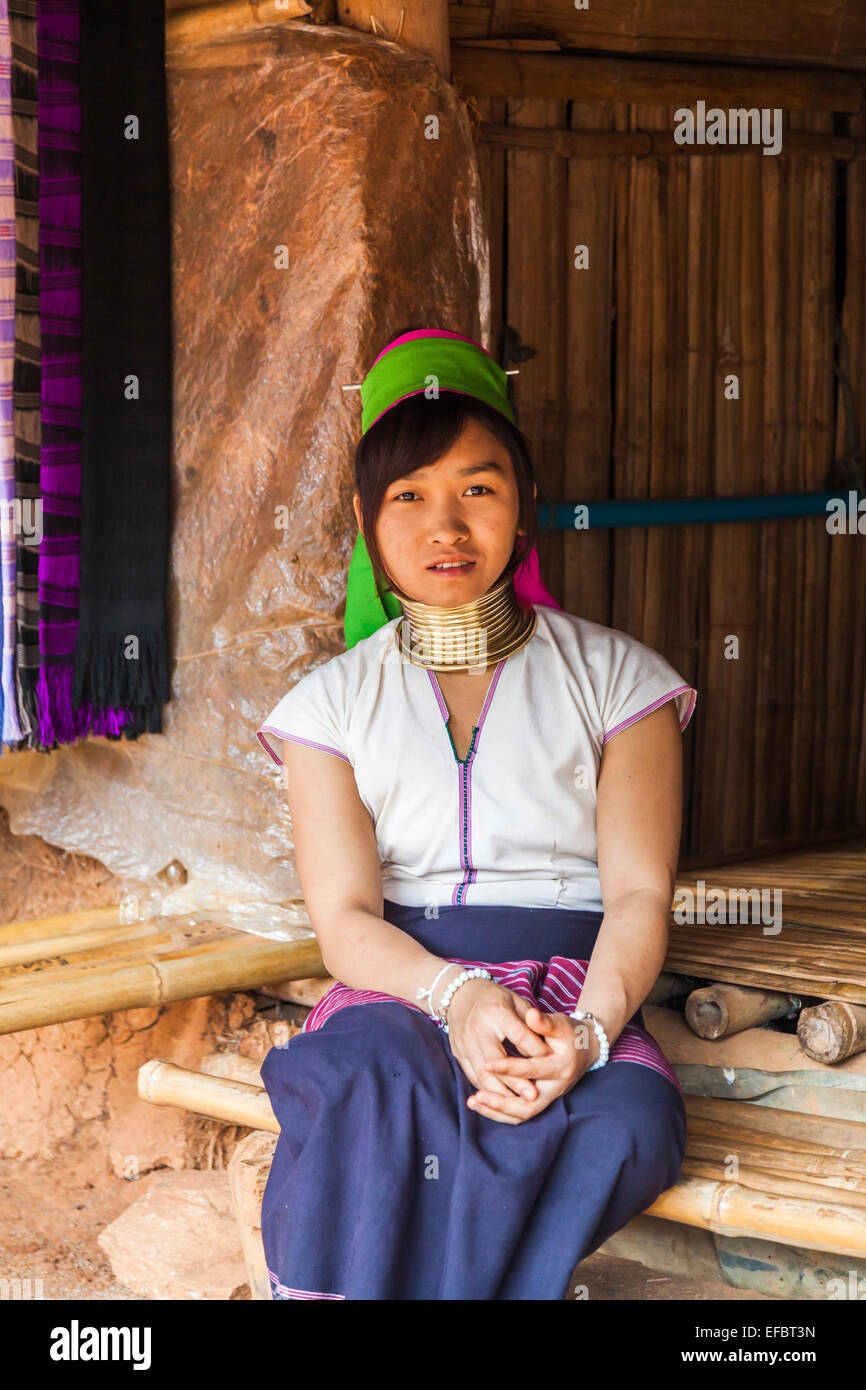 Young Burmese long neck woman with a green headdress sitting in a hut ...
