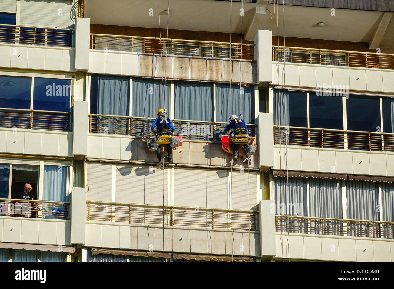 Two men cleaning windows hanging from bosuns chairs on apartment ...