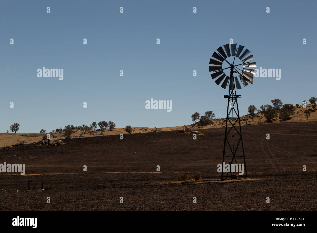 A photograph of a windmill in the aftermath of a bush fire on a dry ...