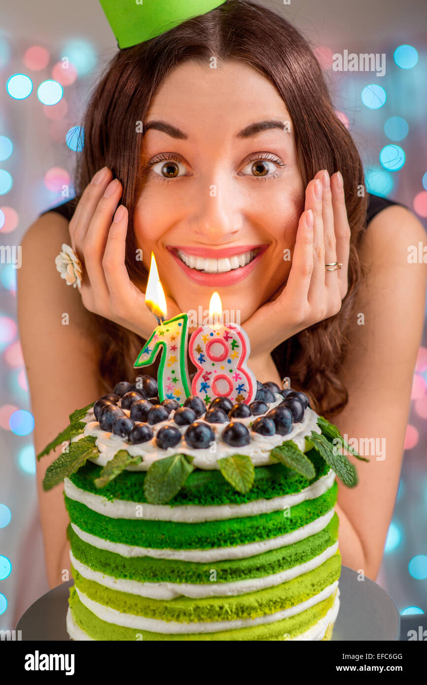Excited eighteen girl with happy birthday cake on festive light ...