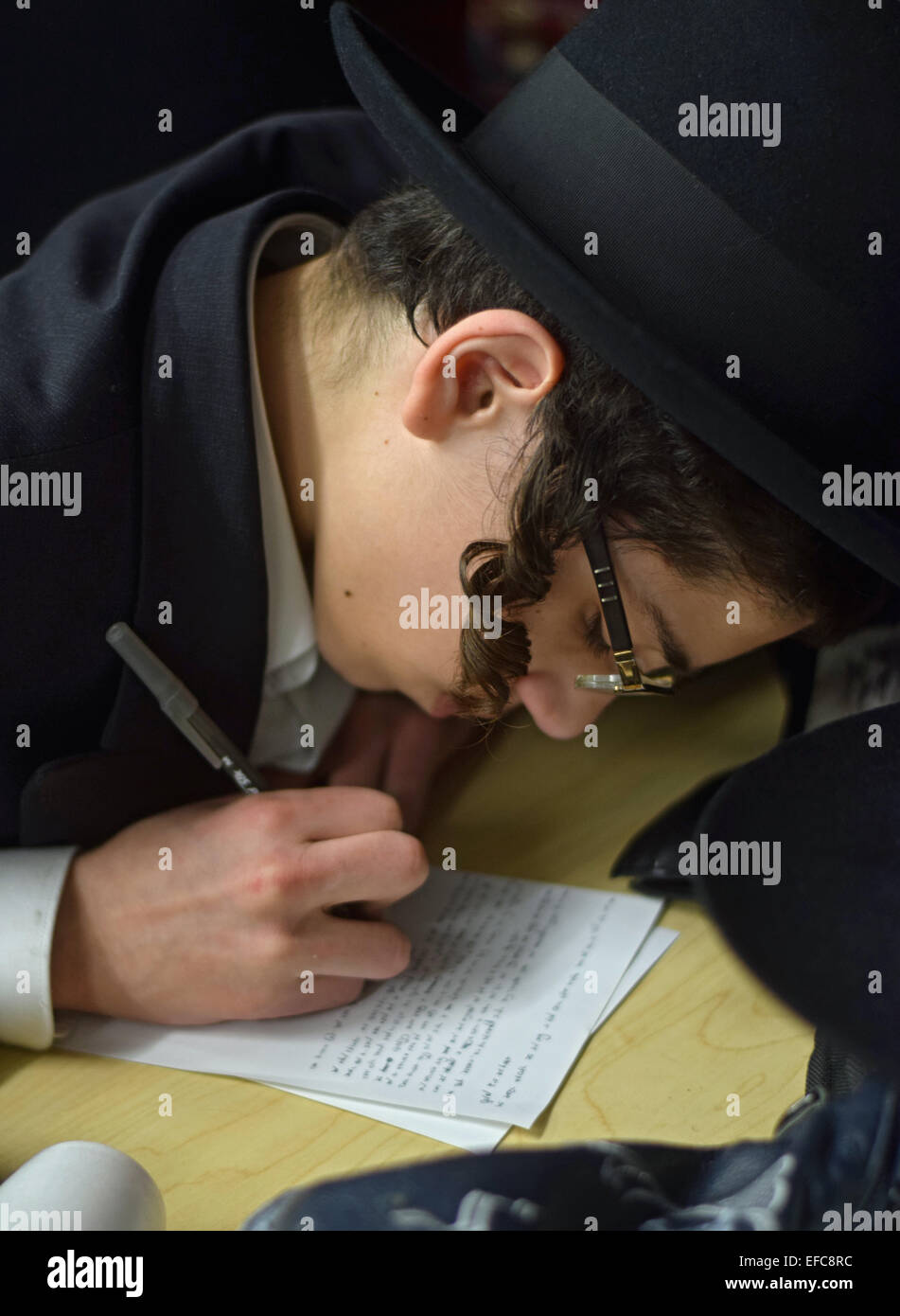 A young religious Jewish boy with long peyot writing a personal prayer ...