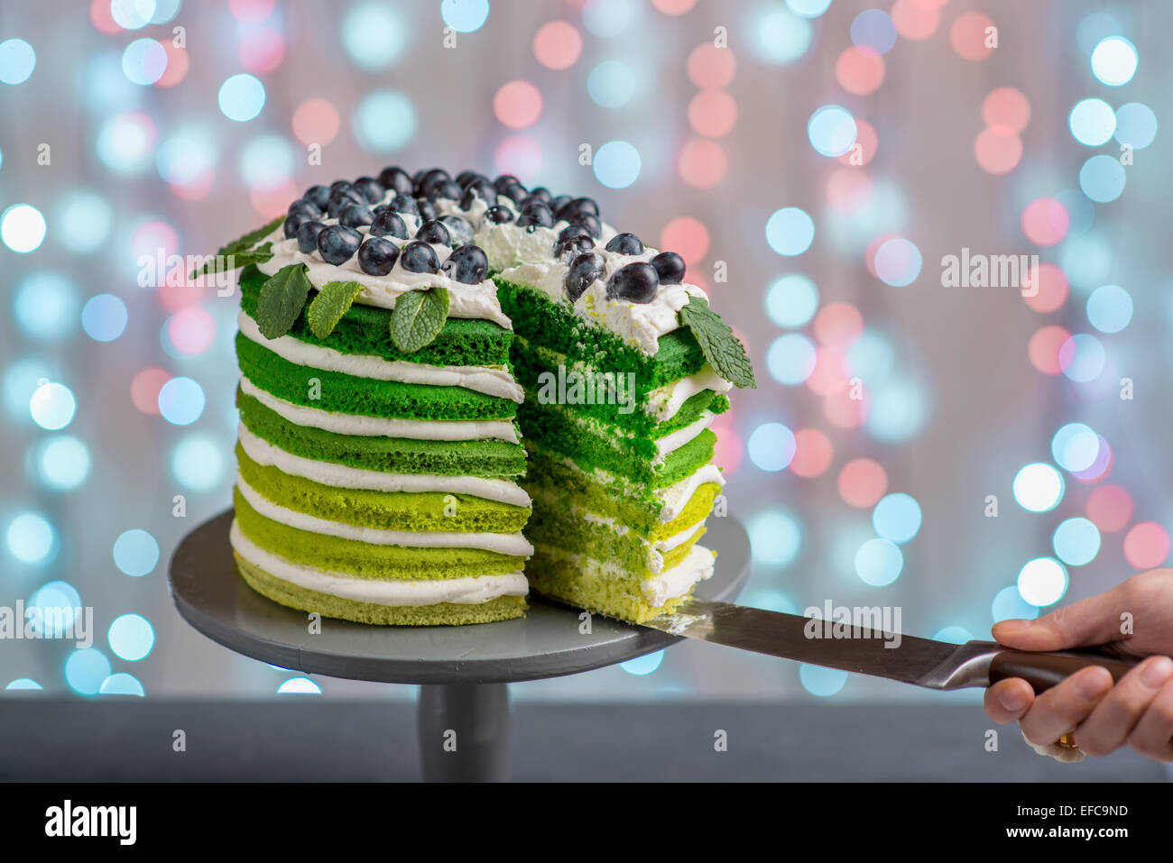 Cutting beautiful green sponge cake on festive background with bokeh ...