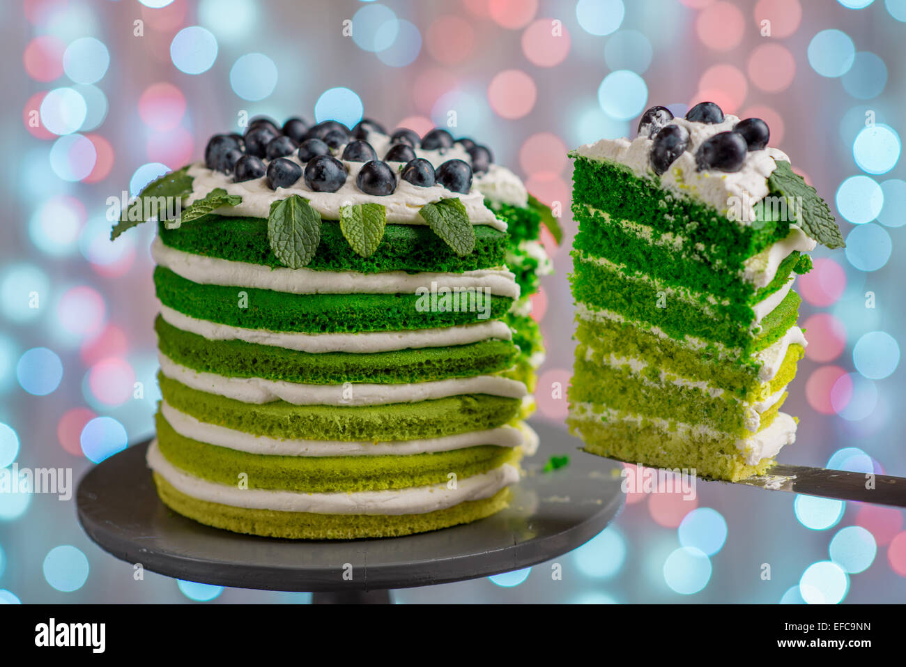 Cutting beautiful green sponge cake on festive background with bokeh ...