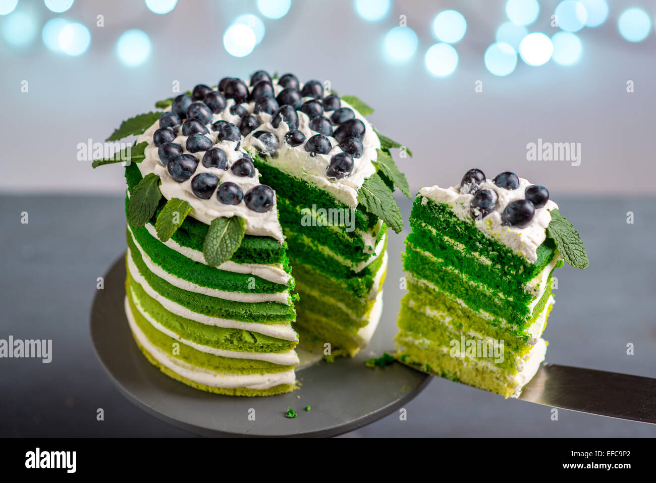 Cutting beautiful green sponge cake on festive background with bokeh ...