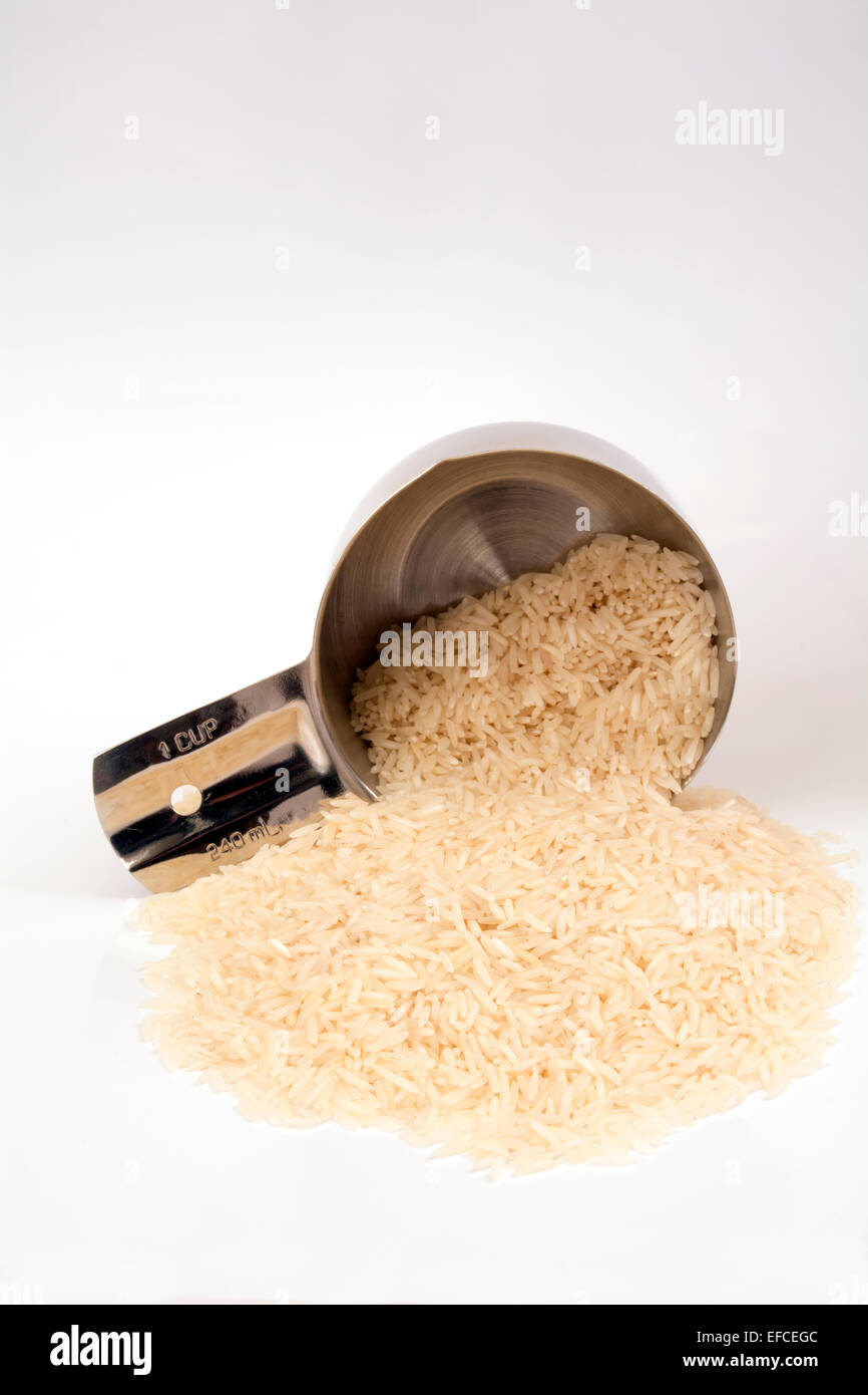 Rice spilling out of a 1 cup measuring cup on a white background as a ...