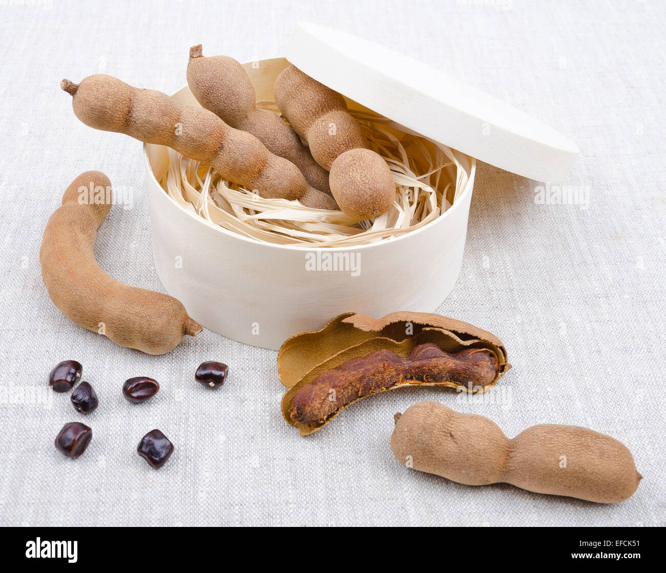 Dried tamarind fruits with seeds in a wooden box on linen. One open pod ...