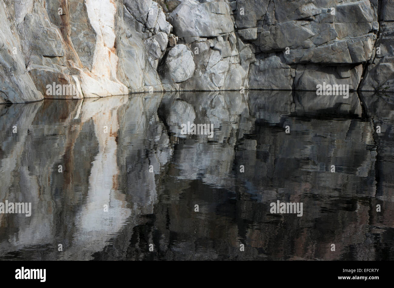 Rock wall reflecting on river Stock Photo - Alamy