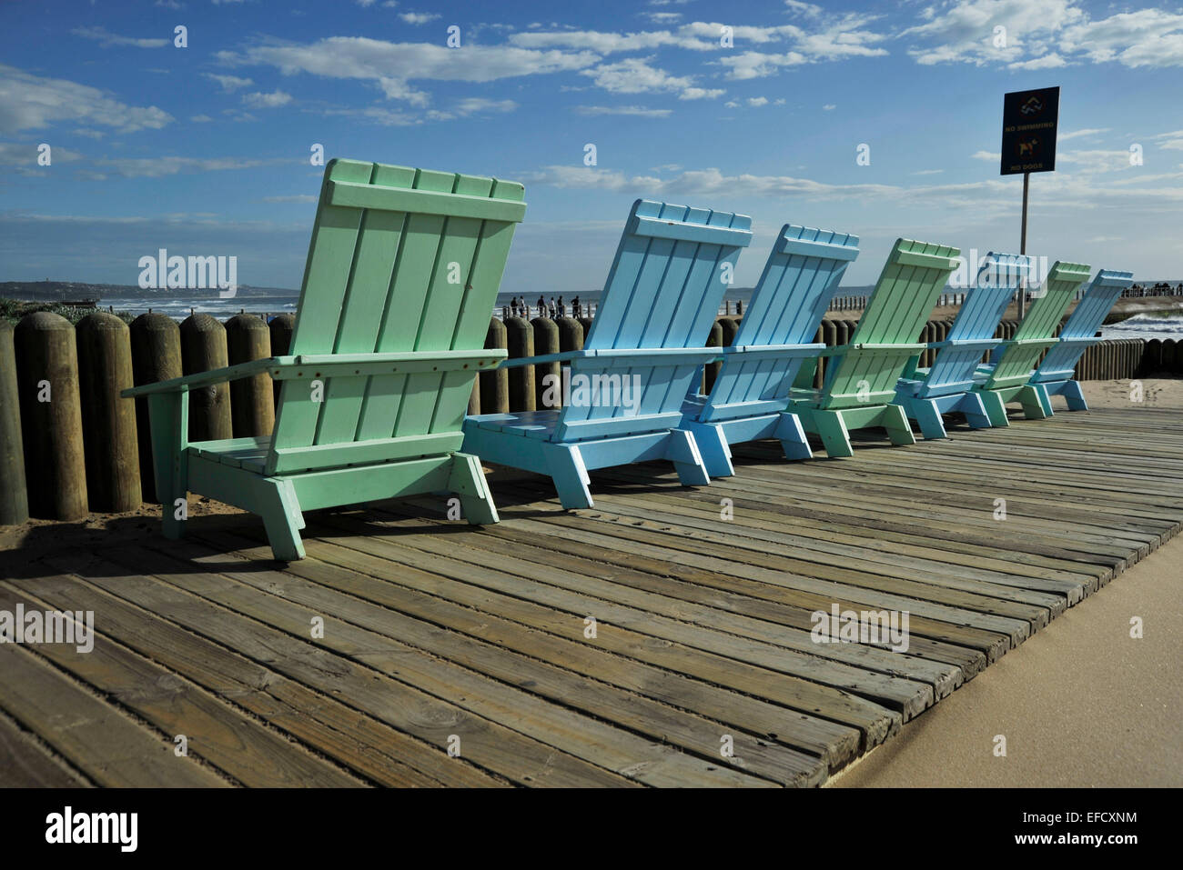 Seven Pastel coloured wooden deckchairs in row, on wood boardwalk at ...