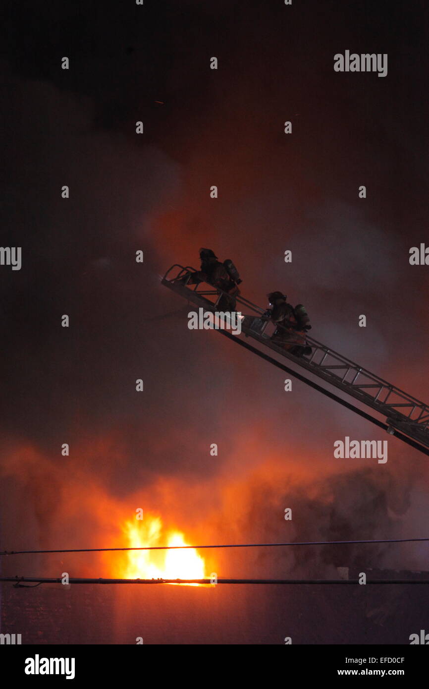 Two firefighters prepare on a ladder above a burning building Stock ...