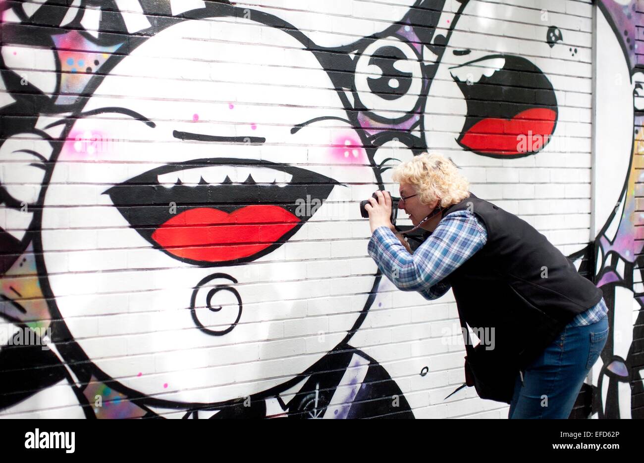 A woman leans to take a photograph of urban street art and graffiti in ...
