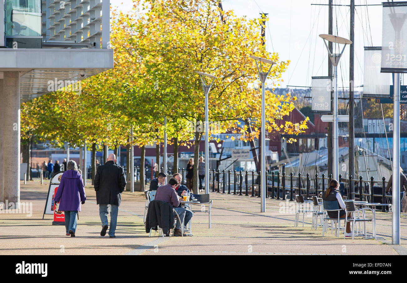 People walk in the warm autumn sunshine under golden trees along ...