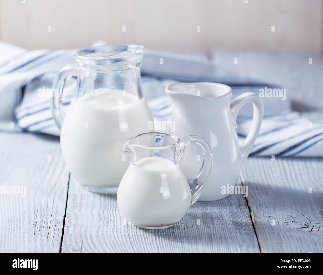 Three milk jars on white wooden background Stock Photo - Alamy