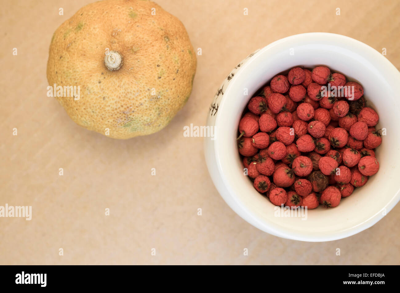 small wild red berries in a porcelain cup and dried lemon on paperboard ...