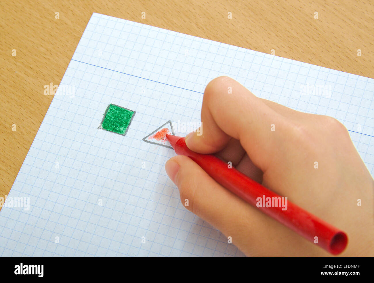 Child drawing red triangle and green square with crayons in classroom ...
