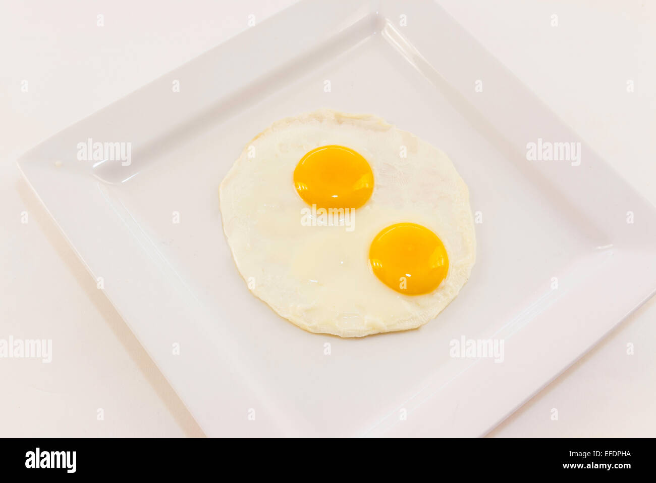 Two fried eggs on a square white plate on a white background Stock ...
