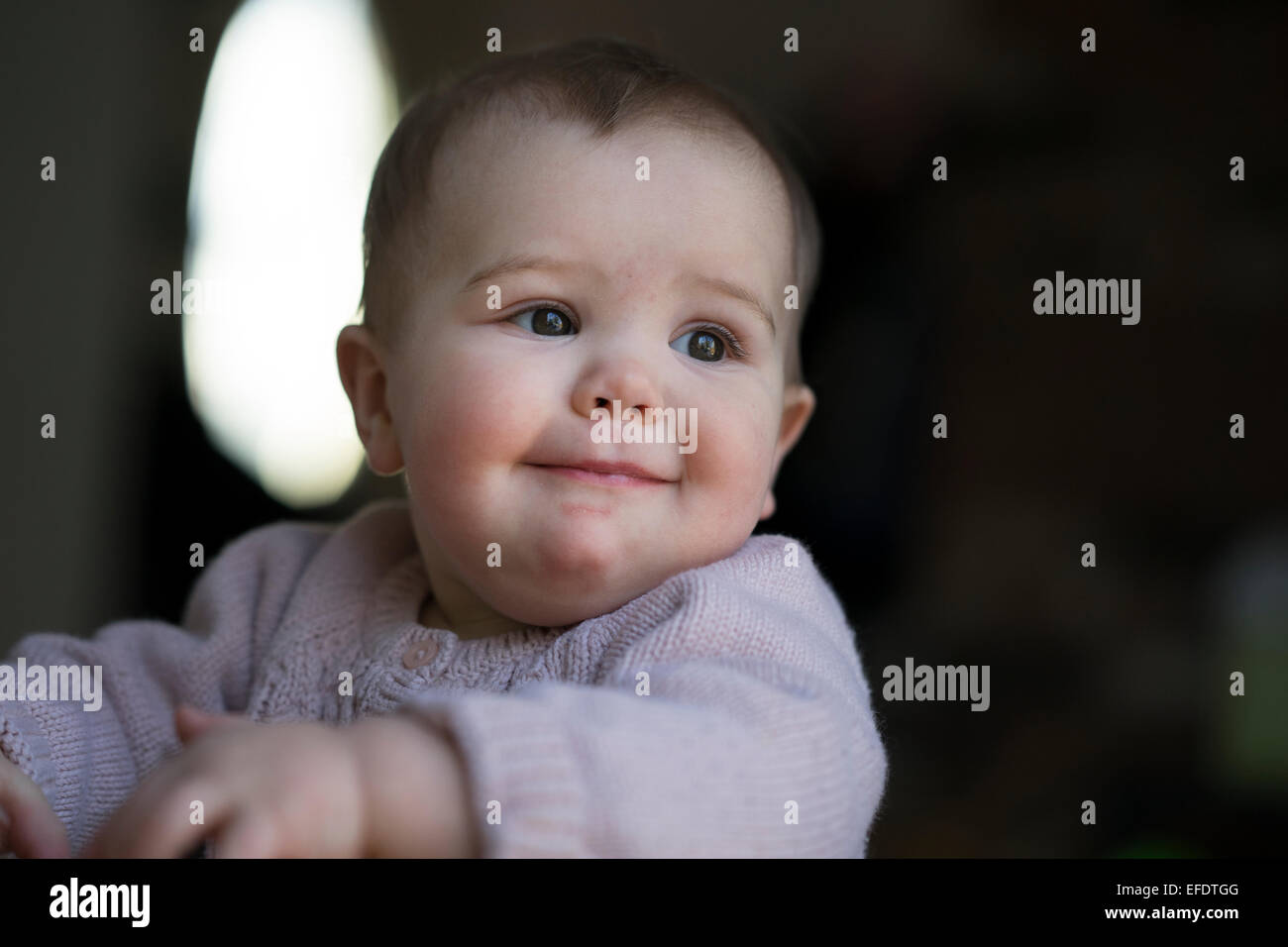 A ten month old baby girl peering out of the window while playing with ...