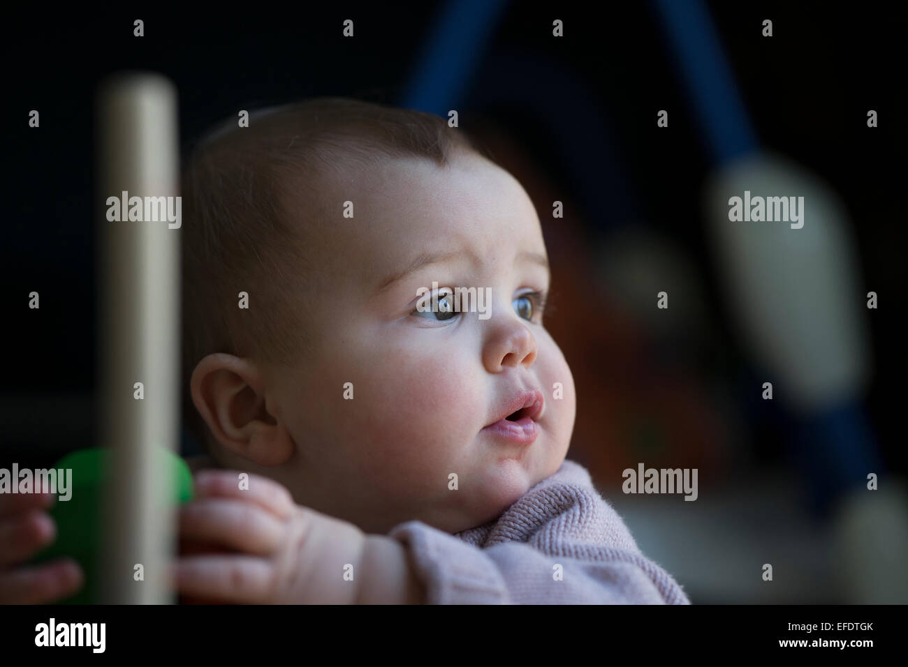 A ten month old baby girl peering out of the window while playing with ...