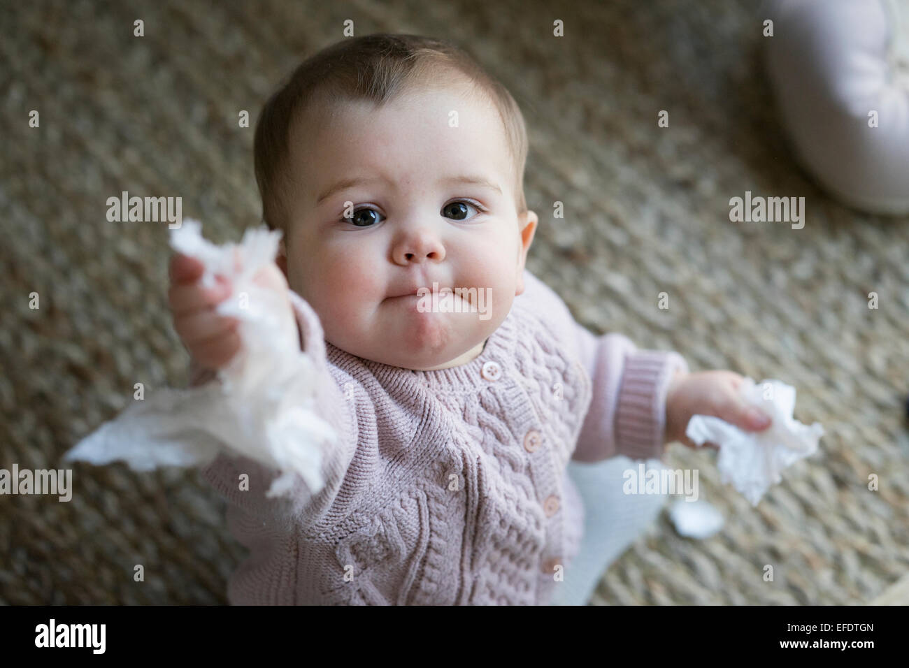 A ten month old baby girl offers a tissue directly towards the camera ...