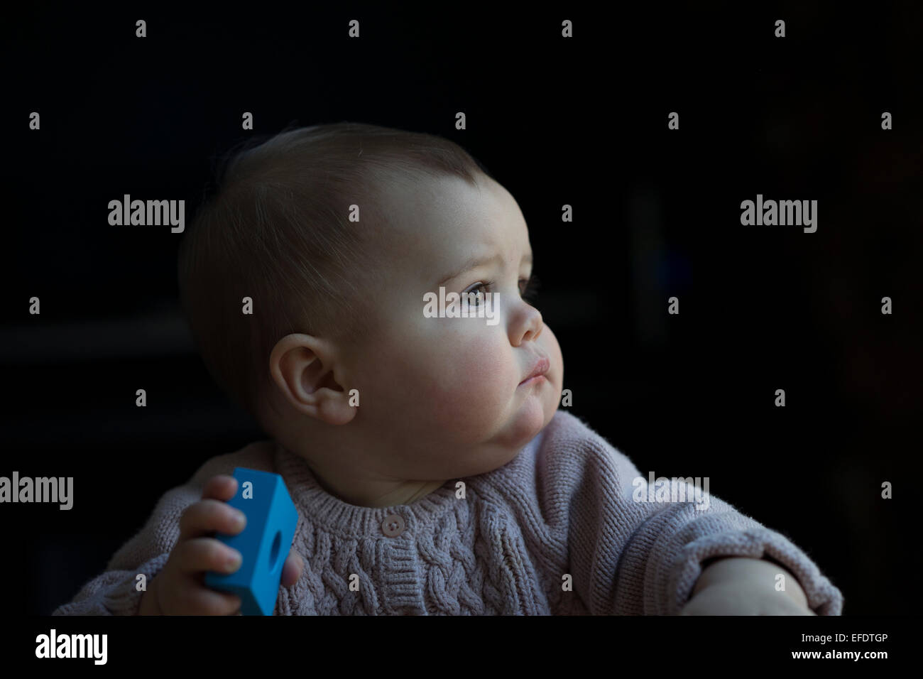 A ten month old baby girl peering out of the window while playing with ...