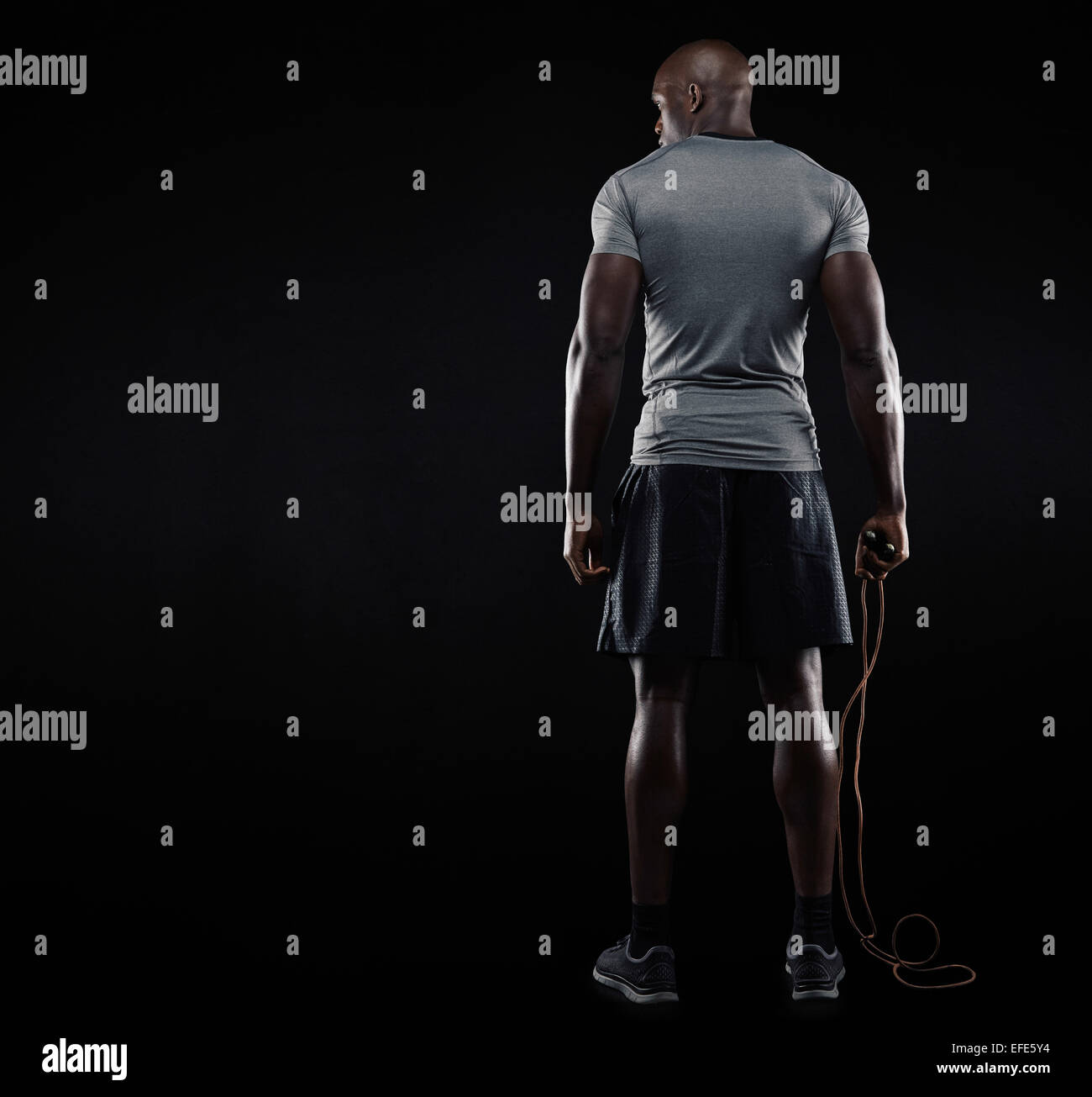 Rear view of muscular man standing with jumping rope on black ...